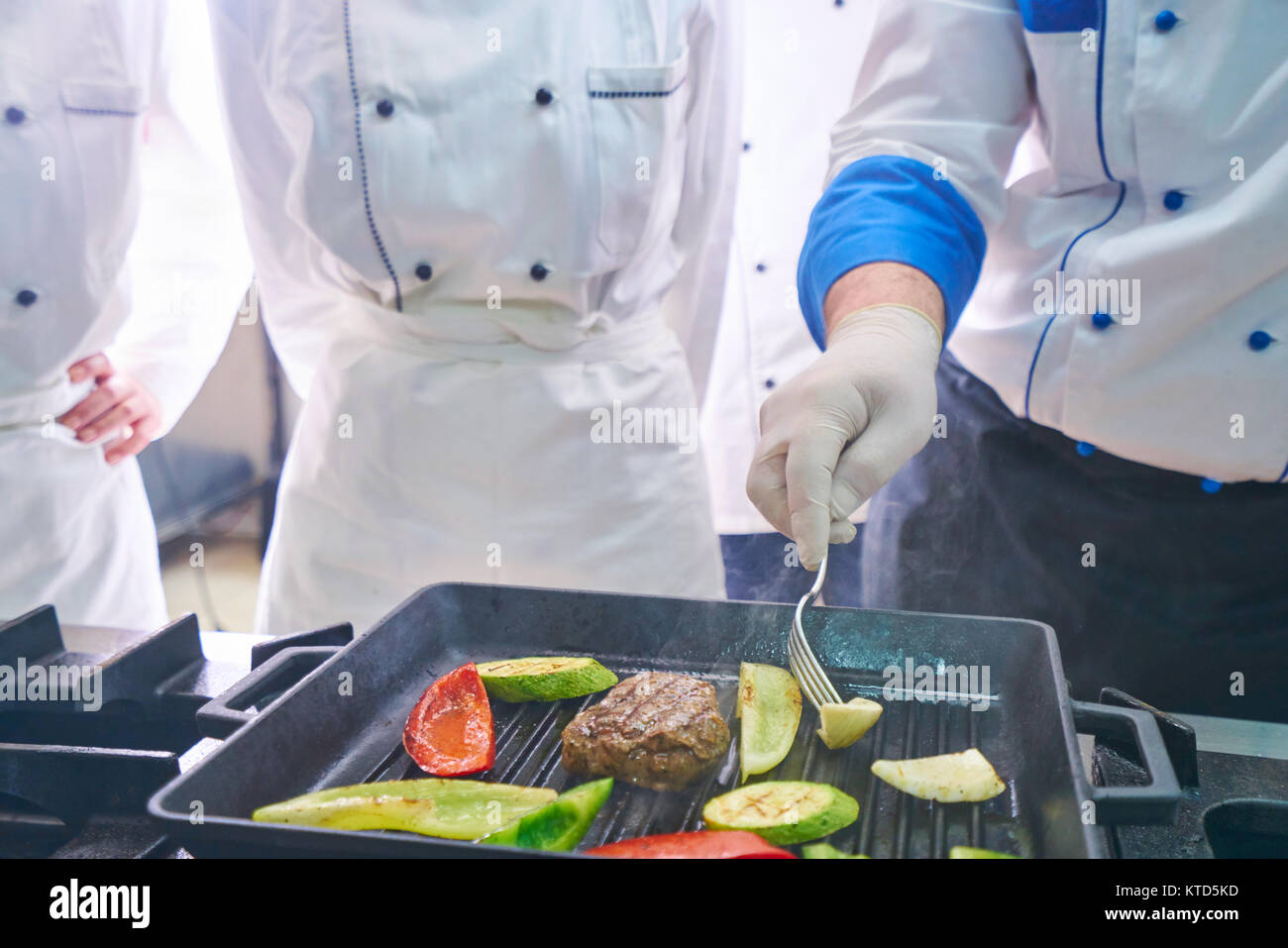 Chef in restaurant kitchen at stove with pan, doing flambe on food ...
