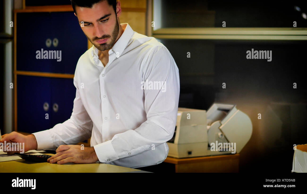 Handsome young man standing at office counter, looking at documents and ...