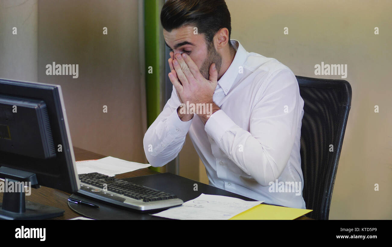 Tired bored young businessman sitting at his desk in front of his ...