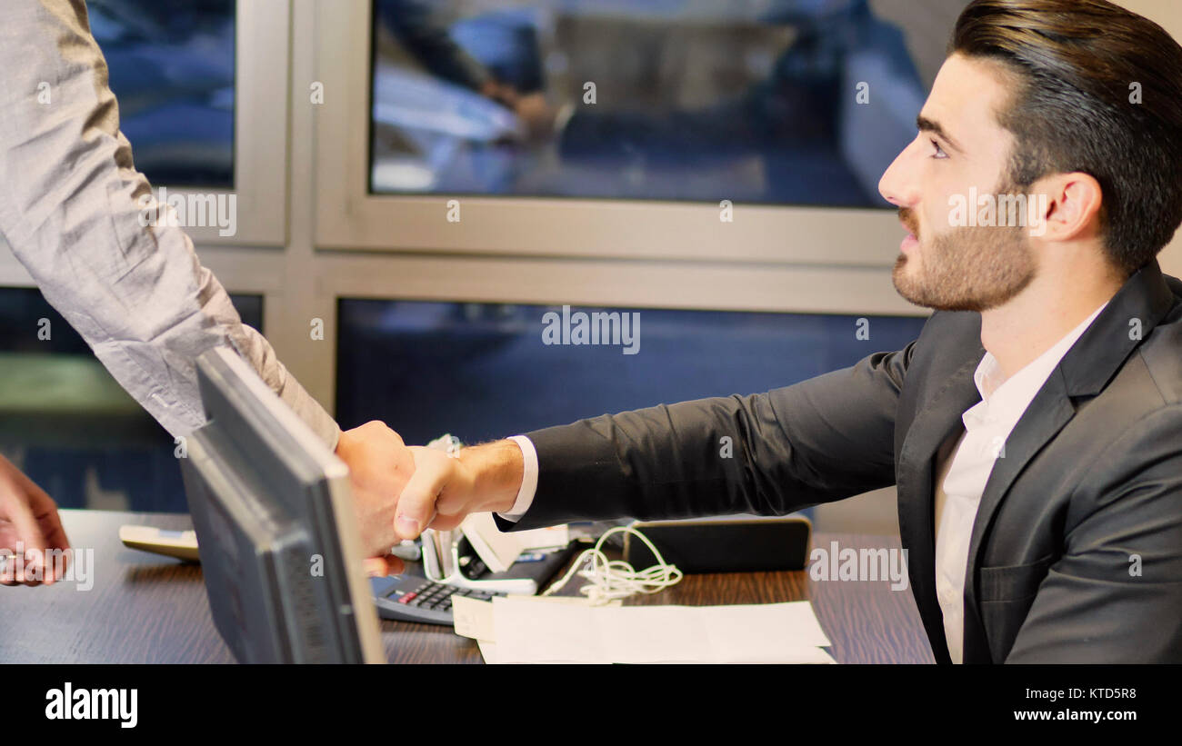Two men in office shaking hands, one is sitting at desk Stock Photo - Alamy