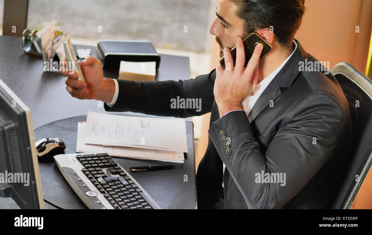 Too much work. Young man using two mobile phones and one desktop ...