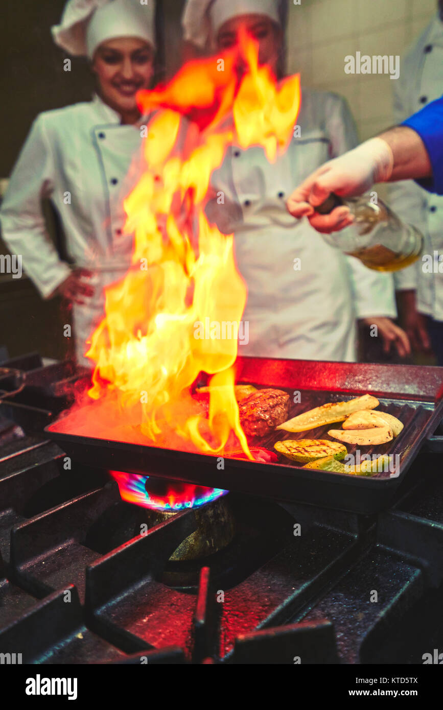 Chef in restaurant kitchen at stove with pan, doing flambe on food ...