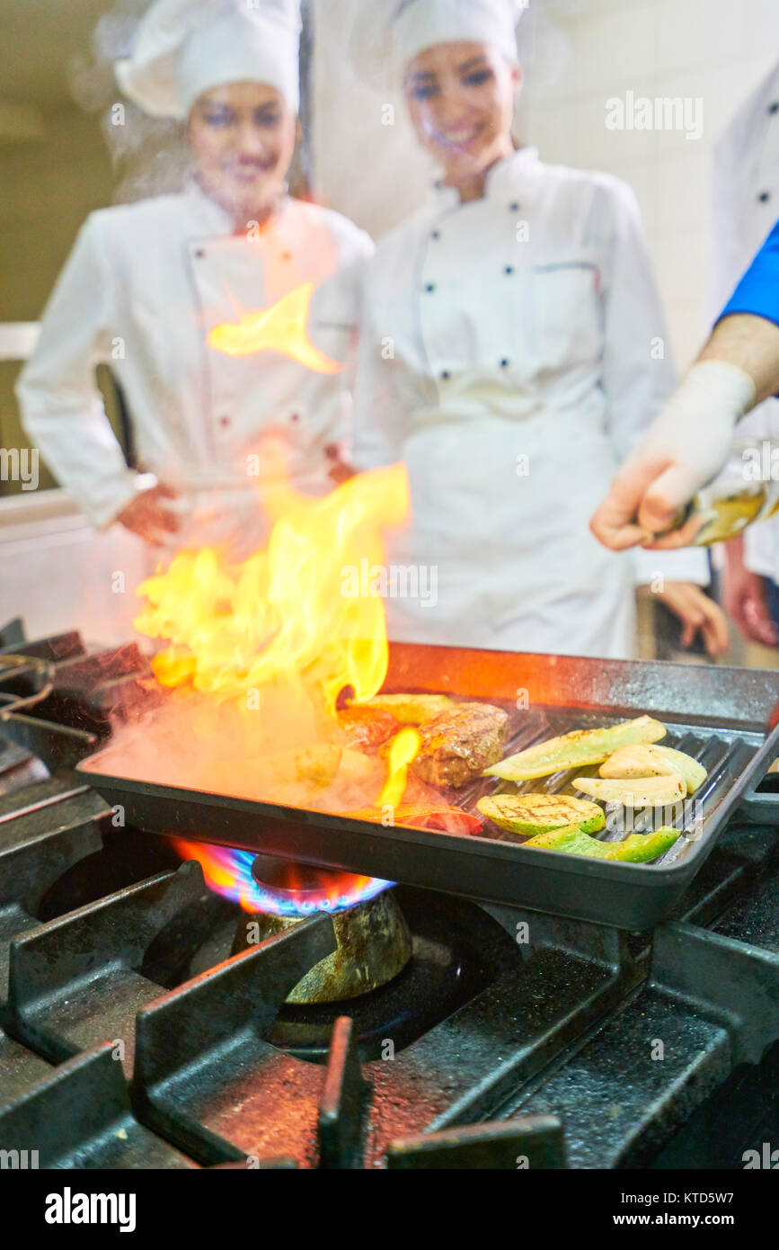 Chef in restaurant kitchen at stove with pan, doing flambe on food ...