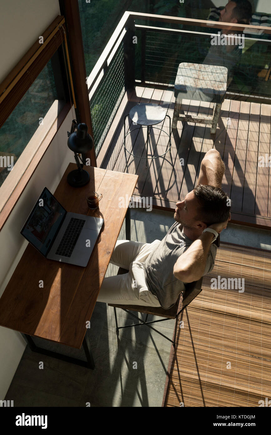Man leaning back and taking a break from working at laptop on desk in ...