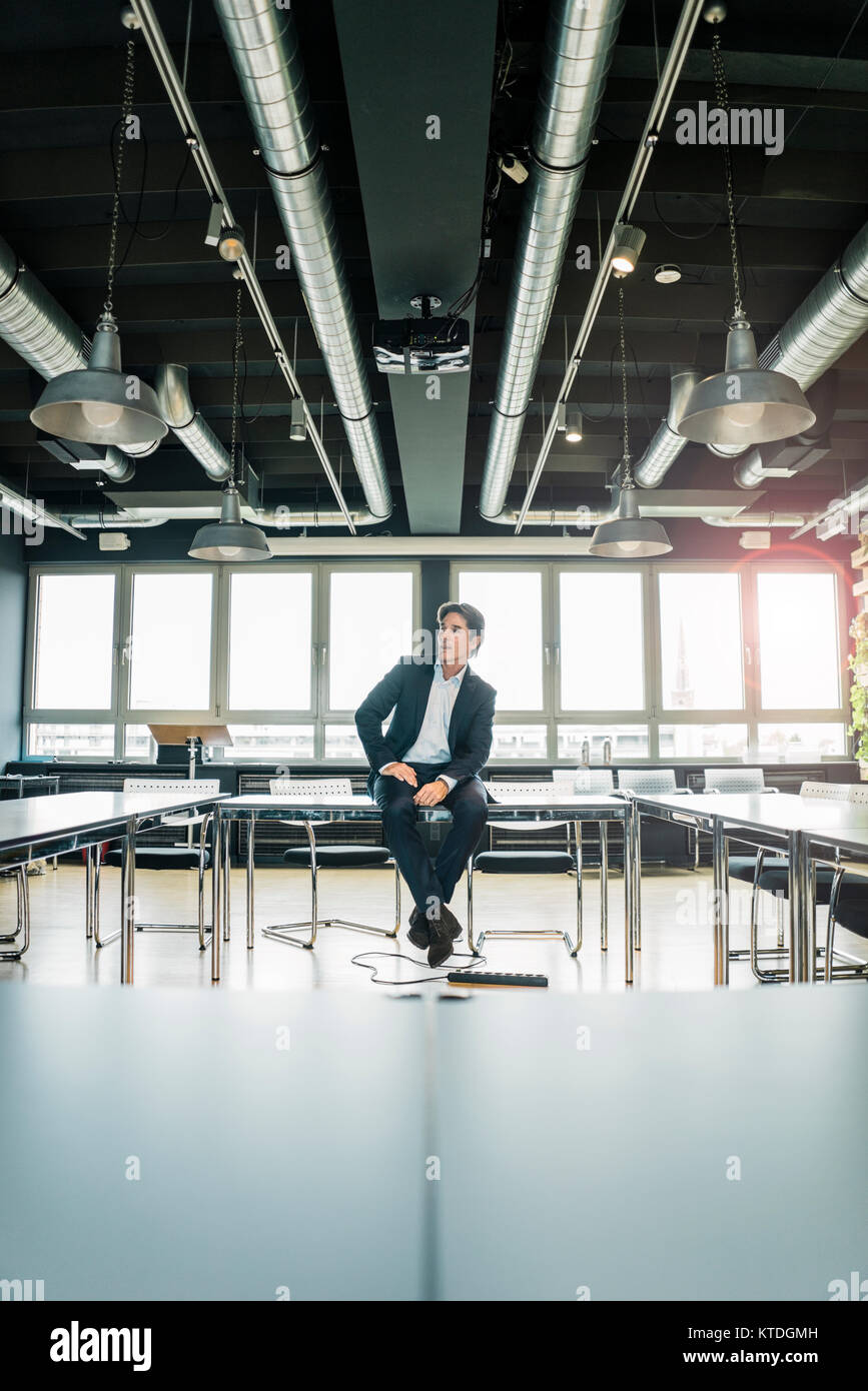 Businessman sitting on table in conference room Stock Photo - Alamy