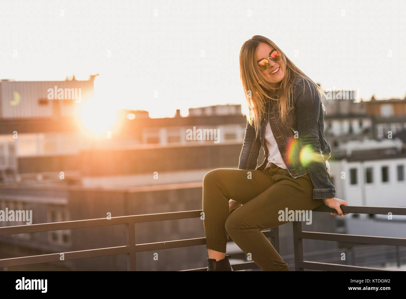 Young woman sitting on railing in the city at sunset Stock Photo - Alamy