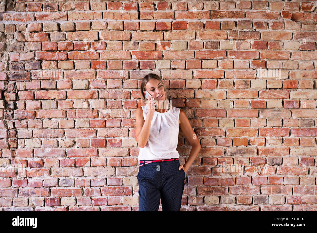 Businesswoman using cell phone at brick wall Stock Photo - Alamy
