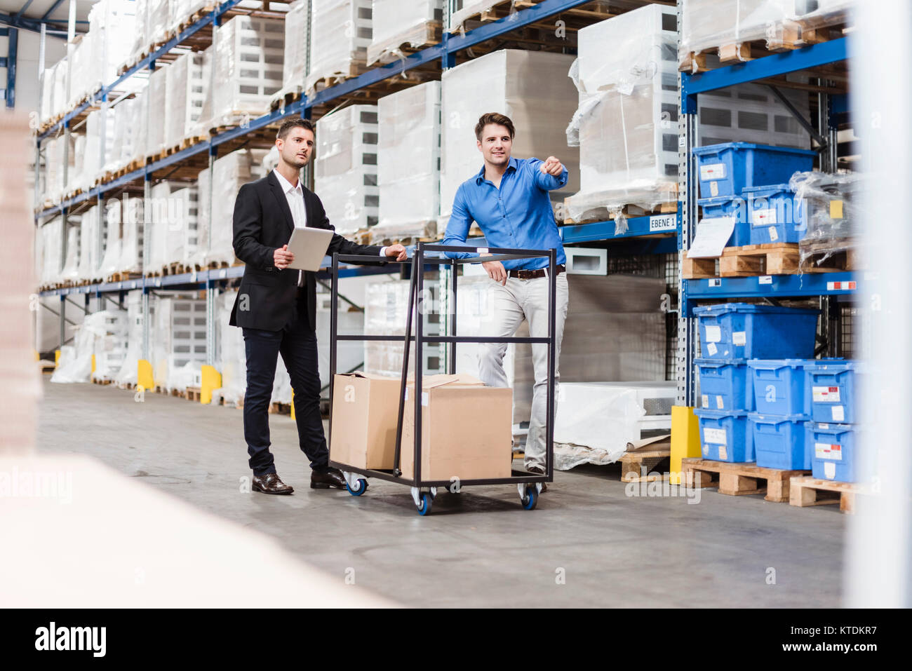 Businessmen in warehouse loading cardboard boxes on transport cart ...