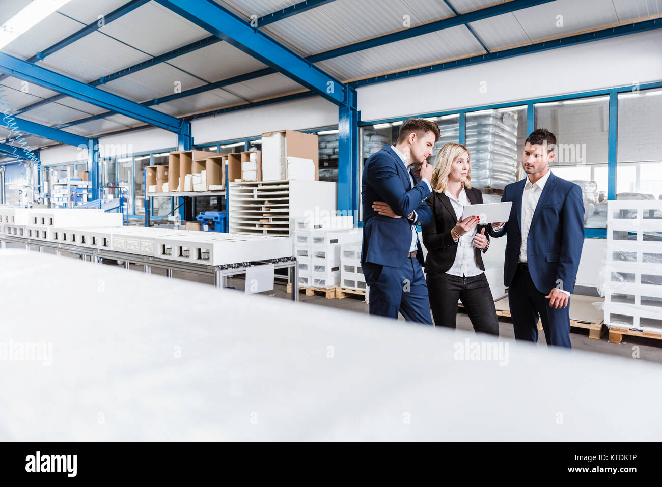 Three business people discussing on shop floor, using digital tablet ...