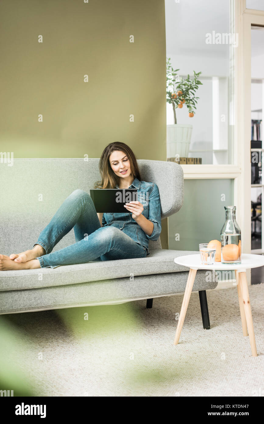 Young woman sitting on the couch using tablet Stock Photo - Alamy