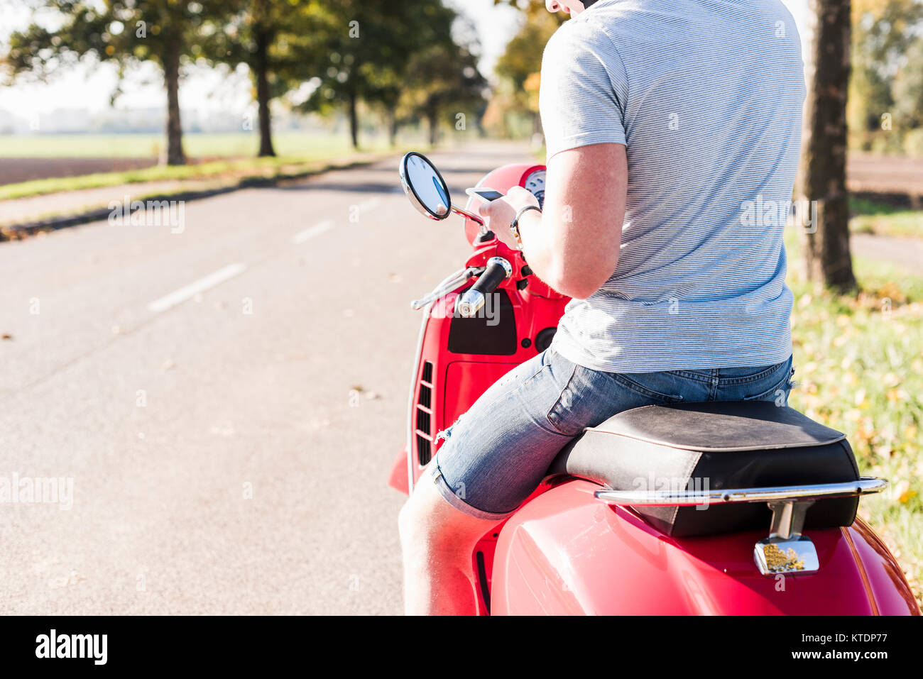 Young man checking cell phone on motor scooter on country road Stock ...