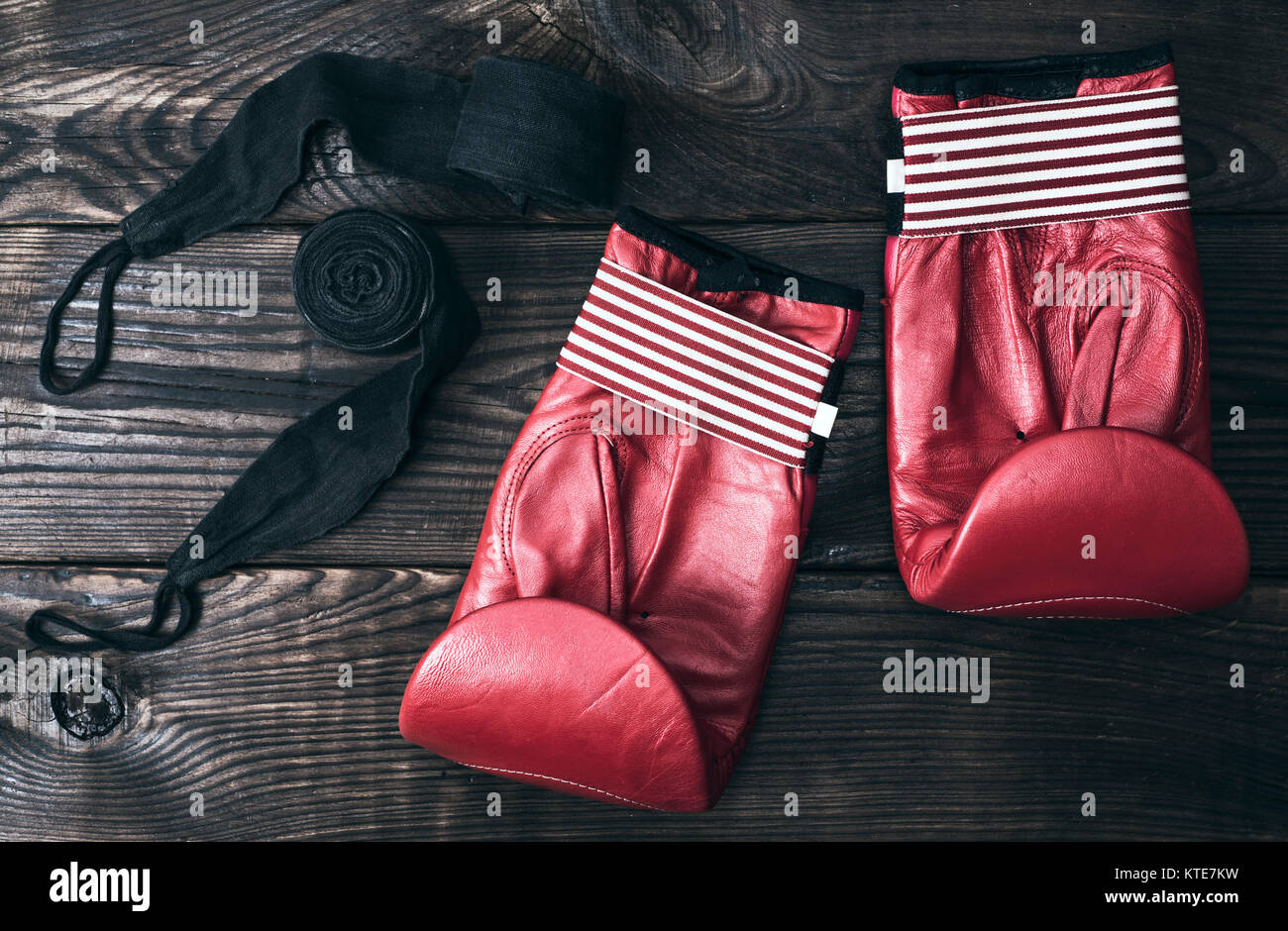 red leather boxing gloves and a black elastic bandage on a brown wooden ...