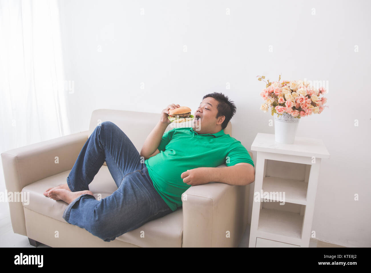 lazy overweight man eating hamburger while laying on a couch Stock ...