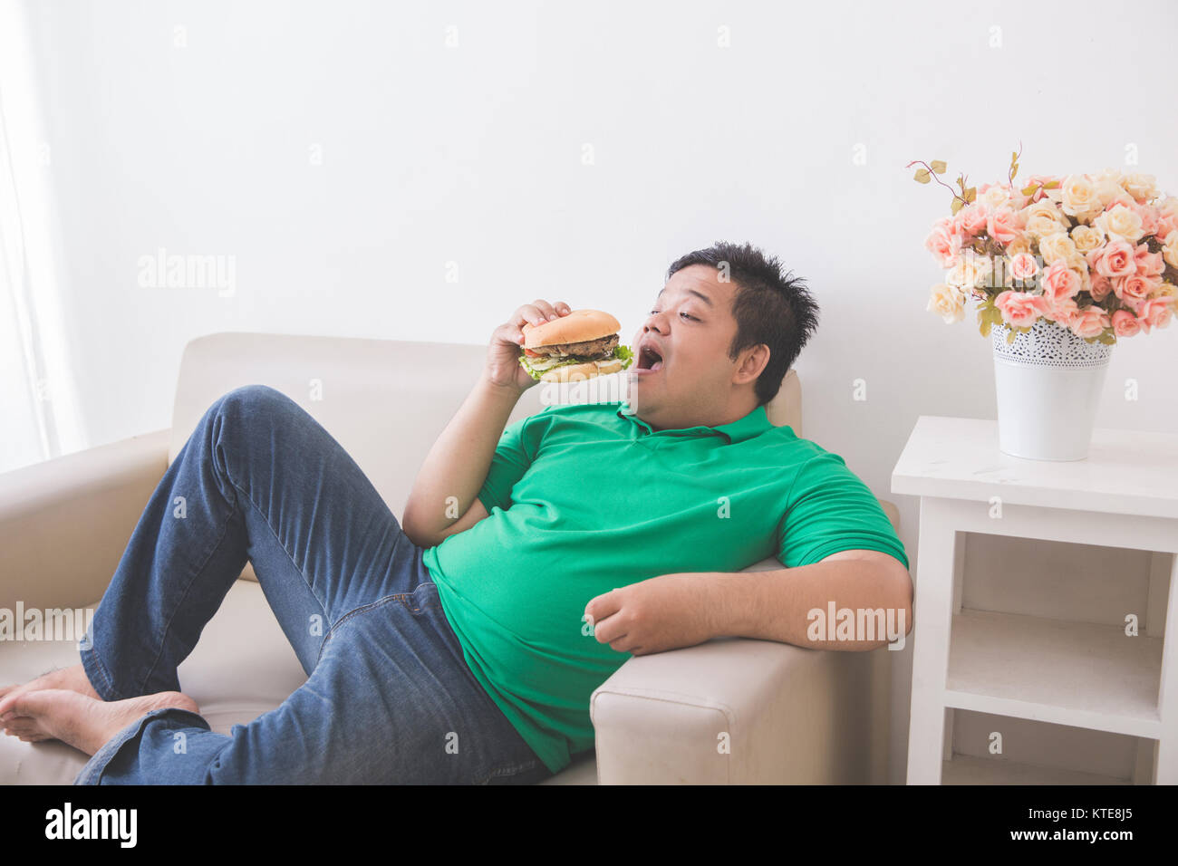 lazy overweight man eating hamburger while laying on a couch Stock ...