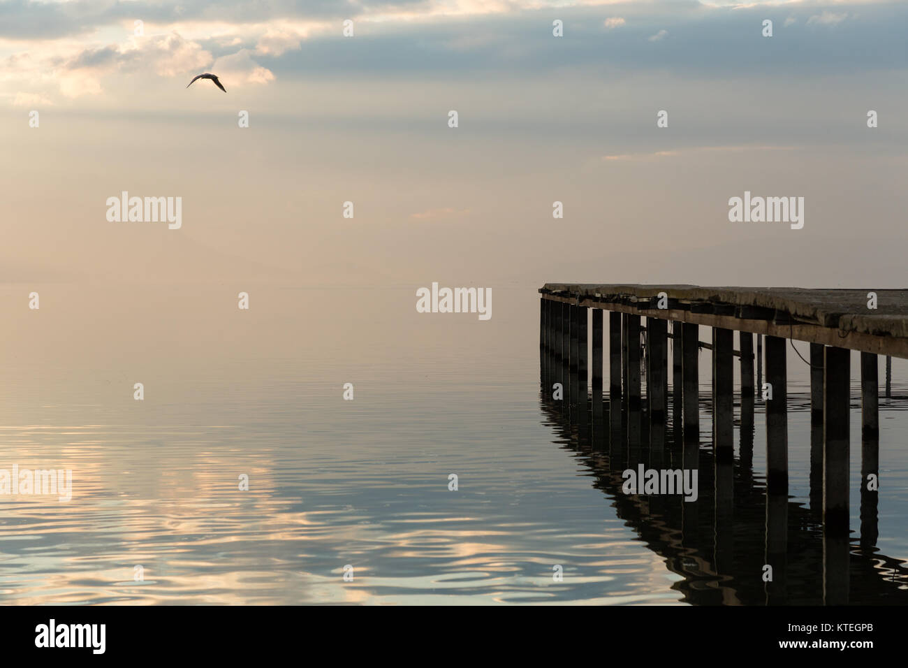 pier and its reflection on a calm lake at sunset Stock Photo - Alamy