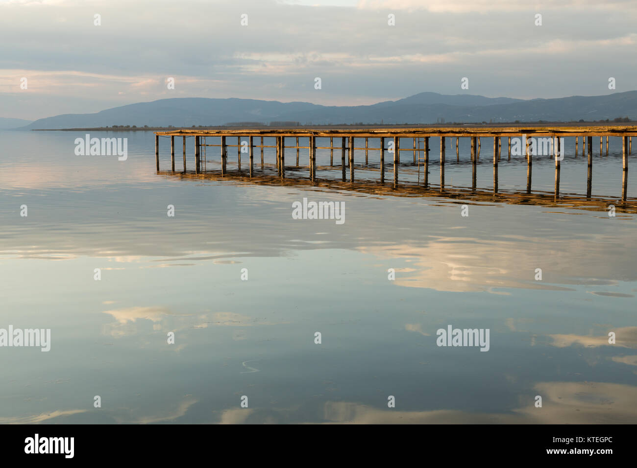pier and its reflection on a calm lake at sunset Stock Photo - Alamy