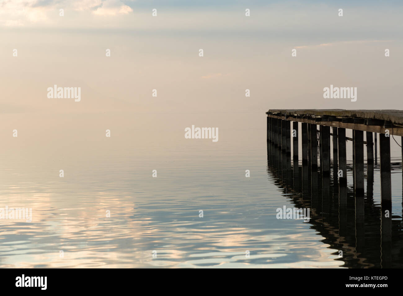 pier and its reflection on a calm lake at sunset Stock Photo - Alamy