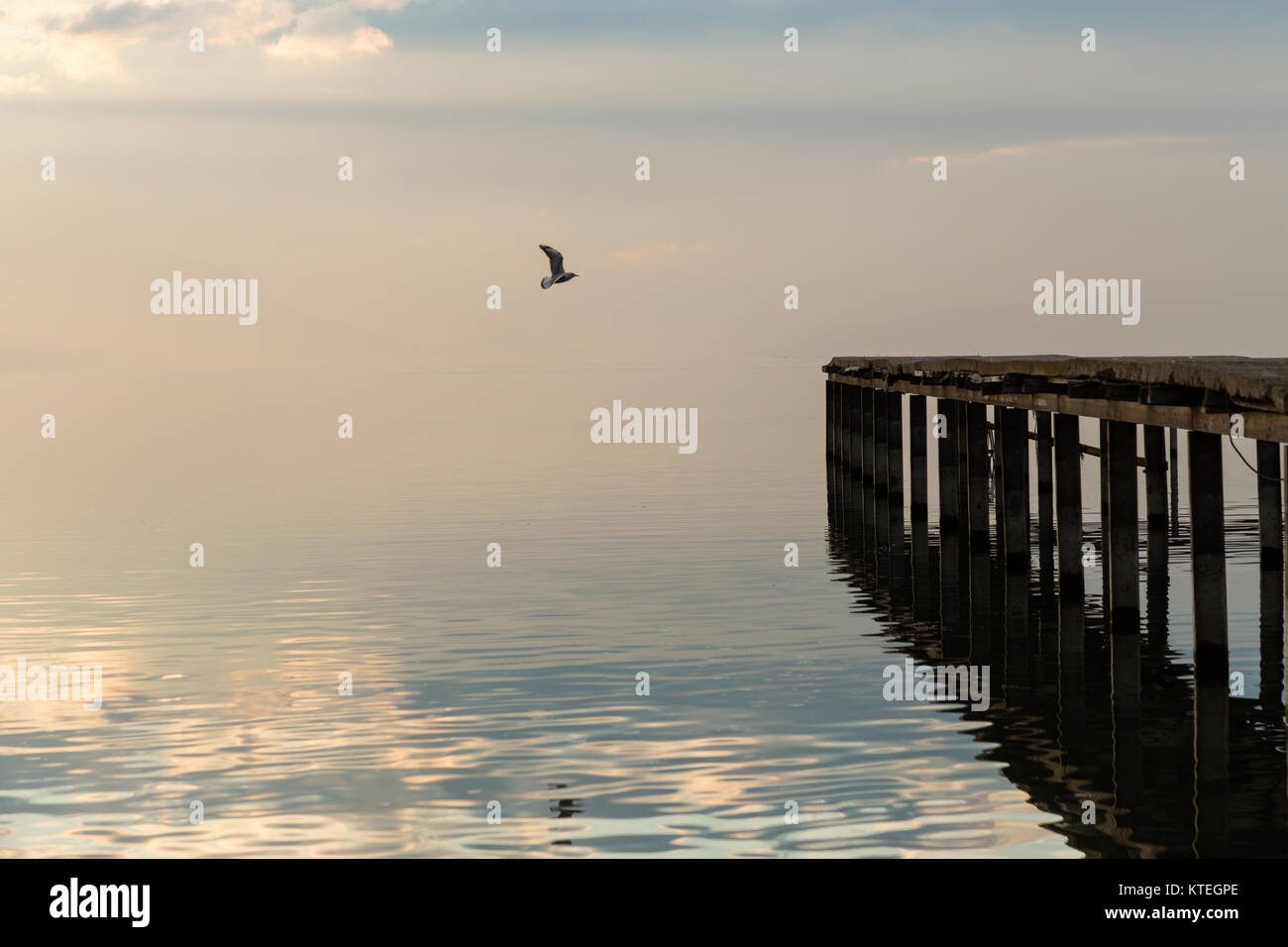 pier and its reflection on a calm lake at sunset Stock Photo - Alamy