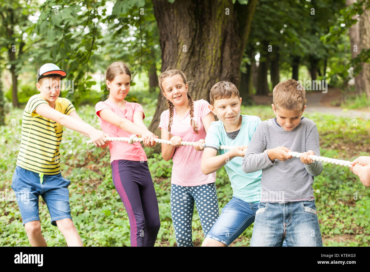 Group of happy smiling kids playing tug-of-war with rope in green park ...