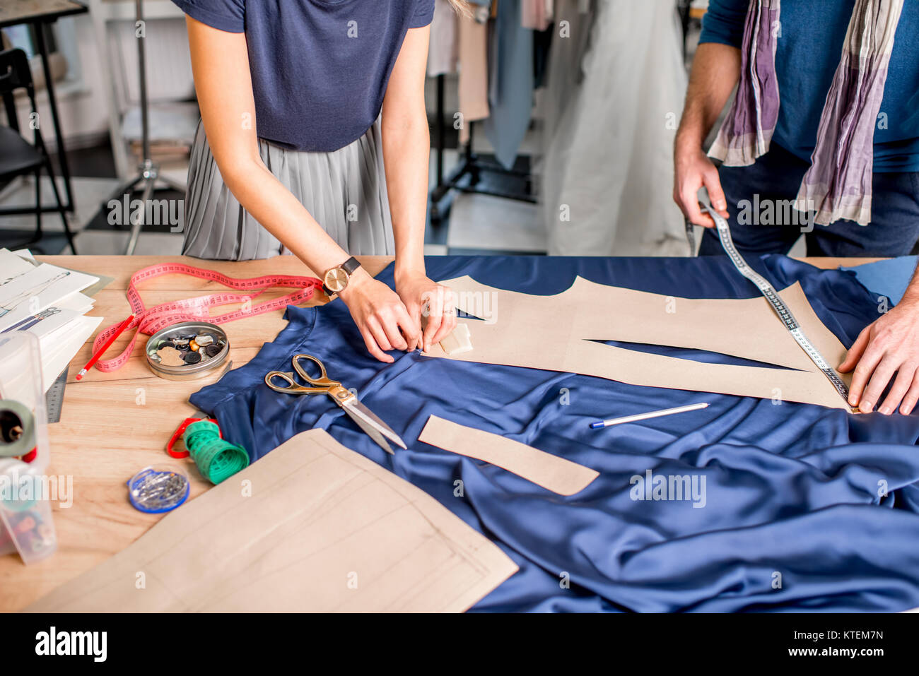 Cutting blue fabric on the table full of tailoring tools. Close-up view ...