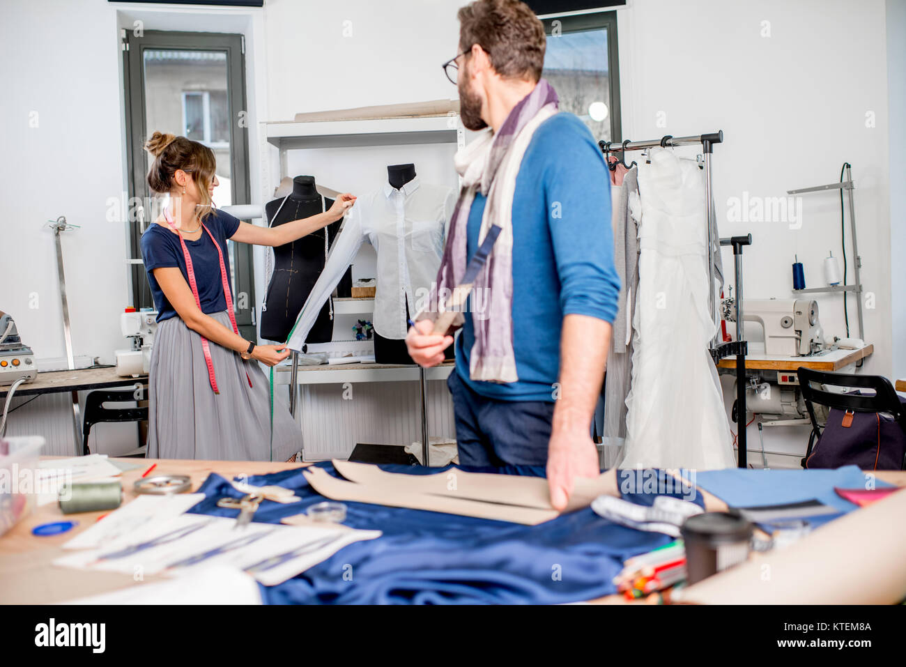 Couple of fashion designers working with fabric and clothing sketches ...