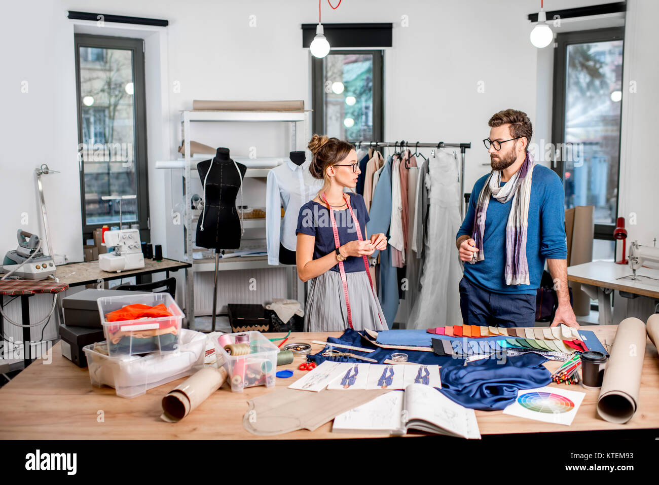 Couple of fashion designers talking at the studio full of tailoring ...