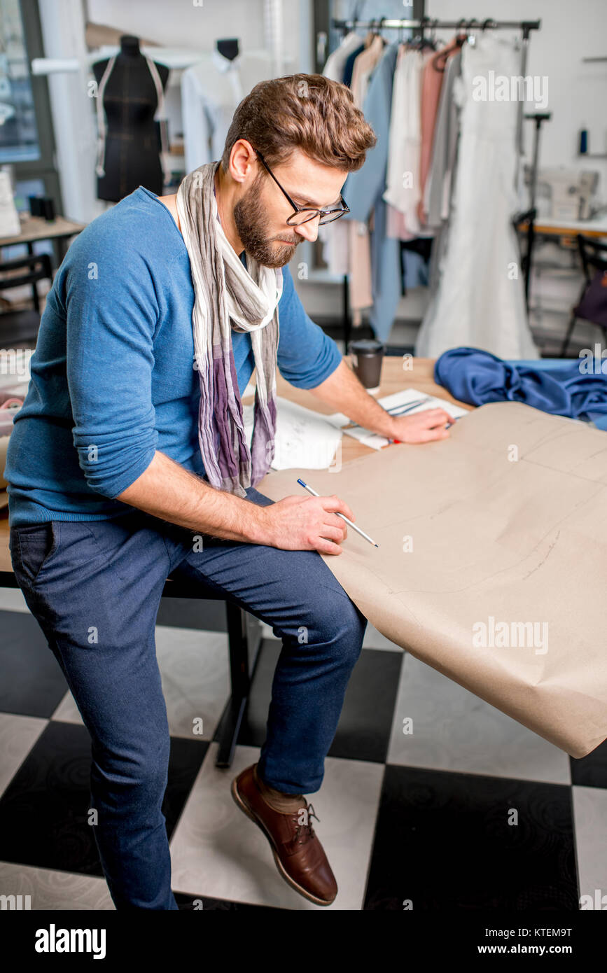 Portrait of a handsome fashion designer sitting with paper sketches at ...