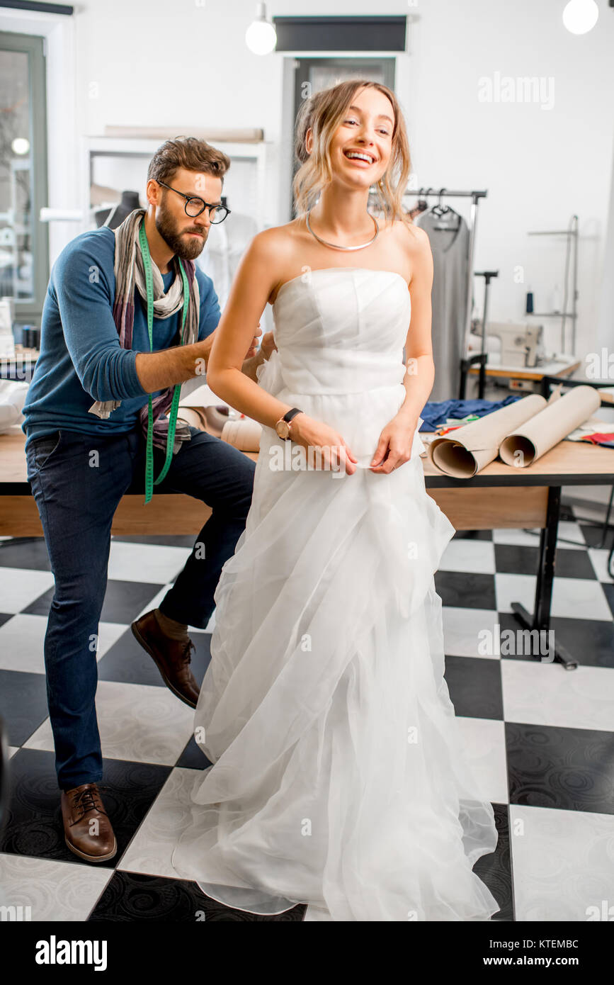 Young woman client fitting wedding dress with man tailor standing at ...