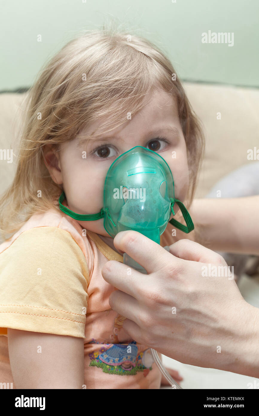 Young child doing inhalation with a nebulizer at home. Mother hands ...