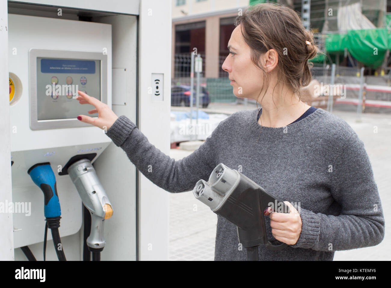 Woman charging electric car at public charging station, holding plug ...