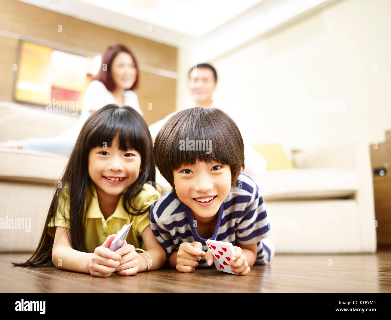 asian brother and sister lying on front on floor with parents in the ...