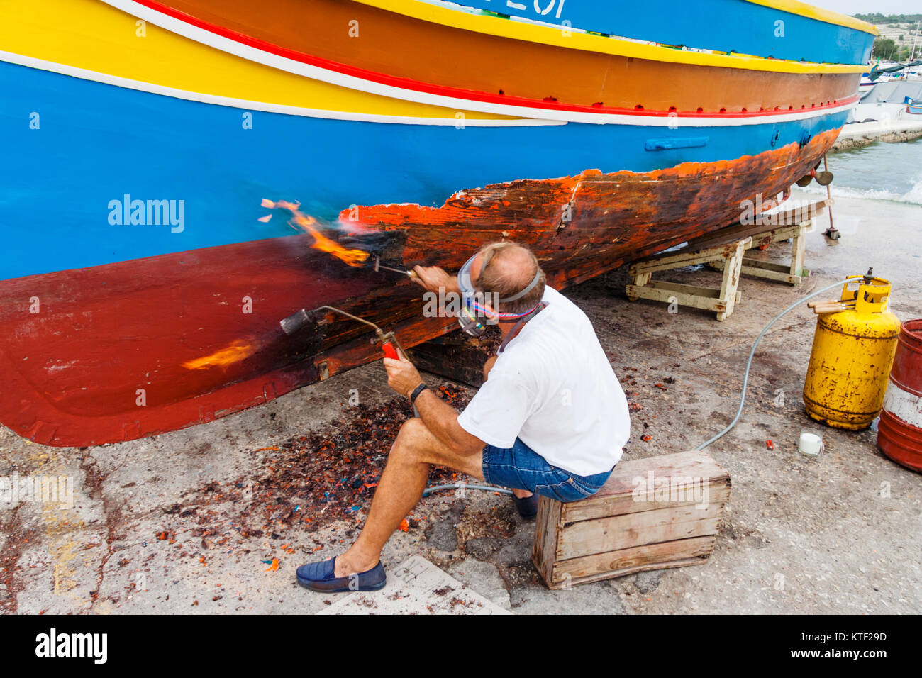 Man repairing a traditional luzzu boat at Marsaxlokk harbour, Malta ...