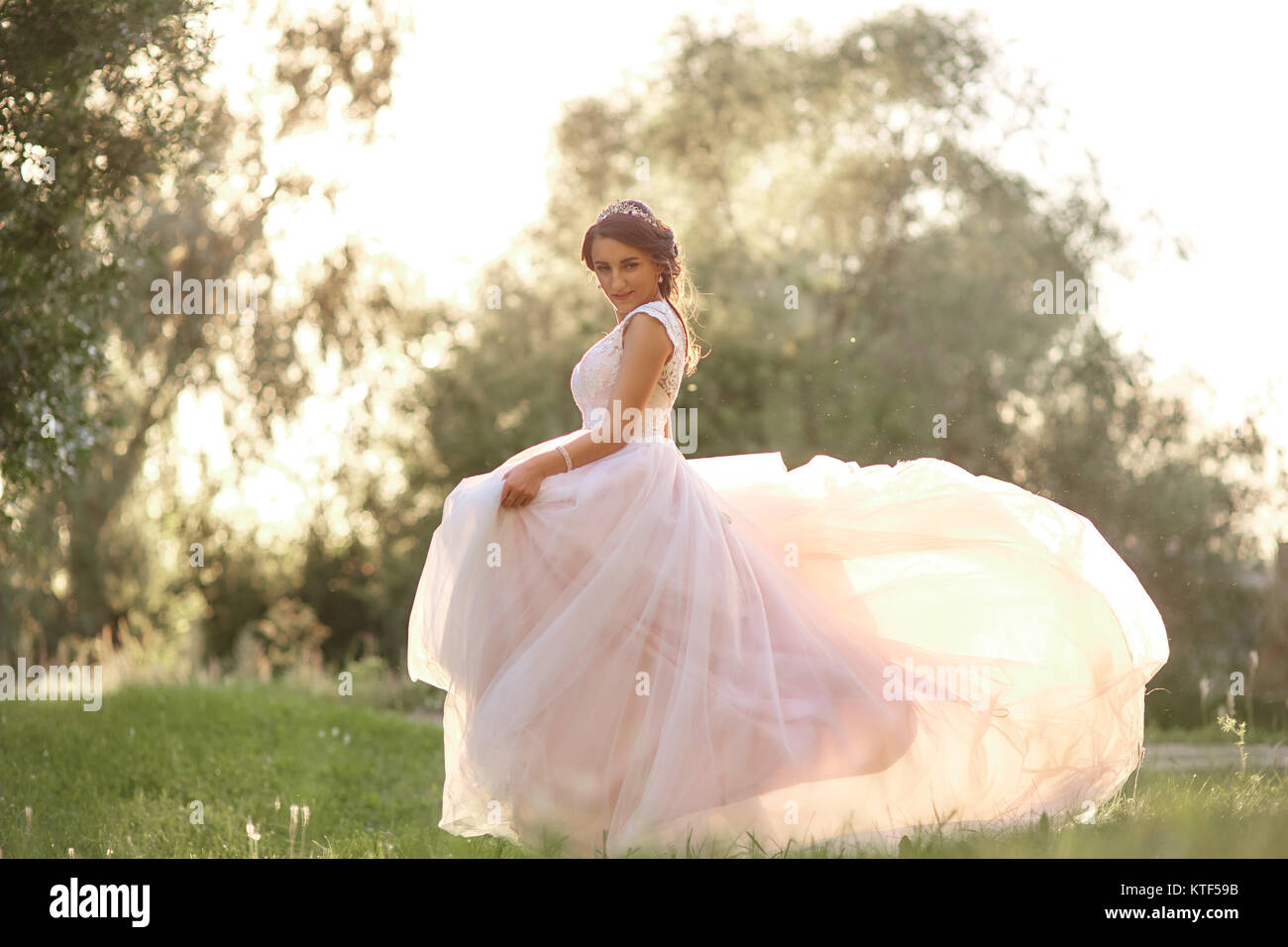 the bride in a long dress is spinning in the alley in the park on a ...