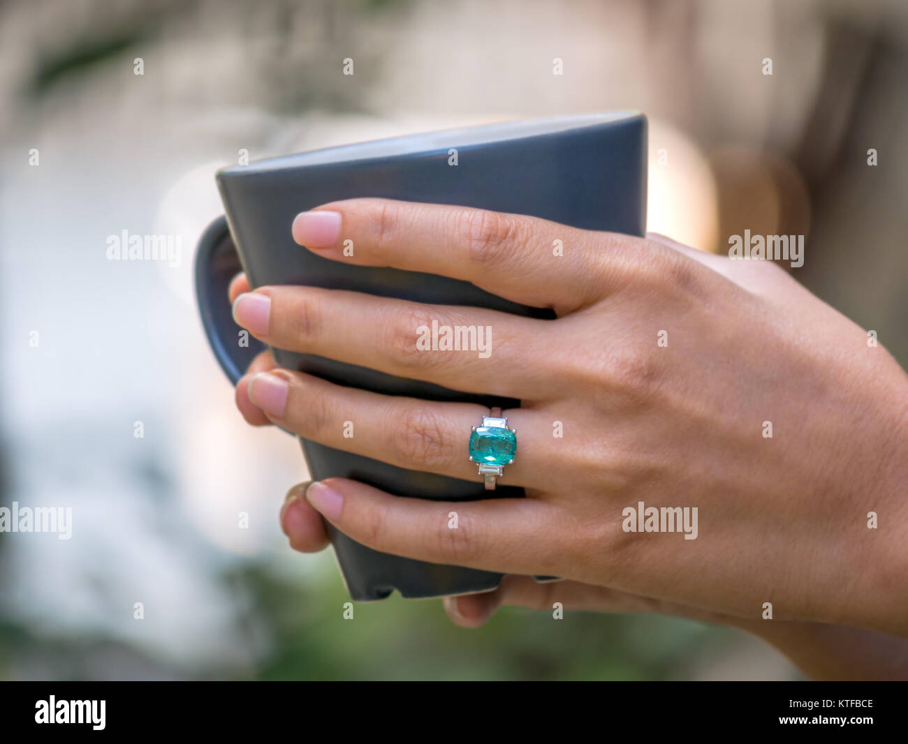 Closup female hand holding coffee cup and wearing green gem ring with ...