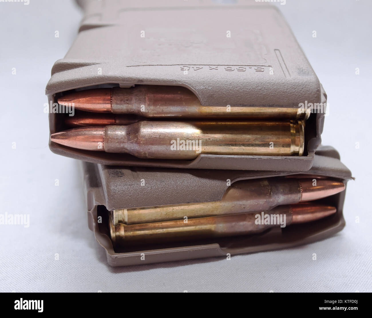 Two loaded .223 rifle magazines stacked on top of each other on a white ...