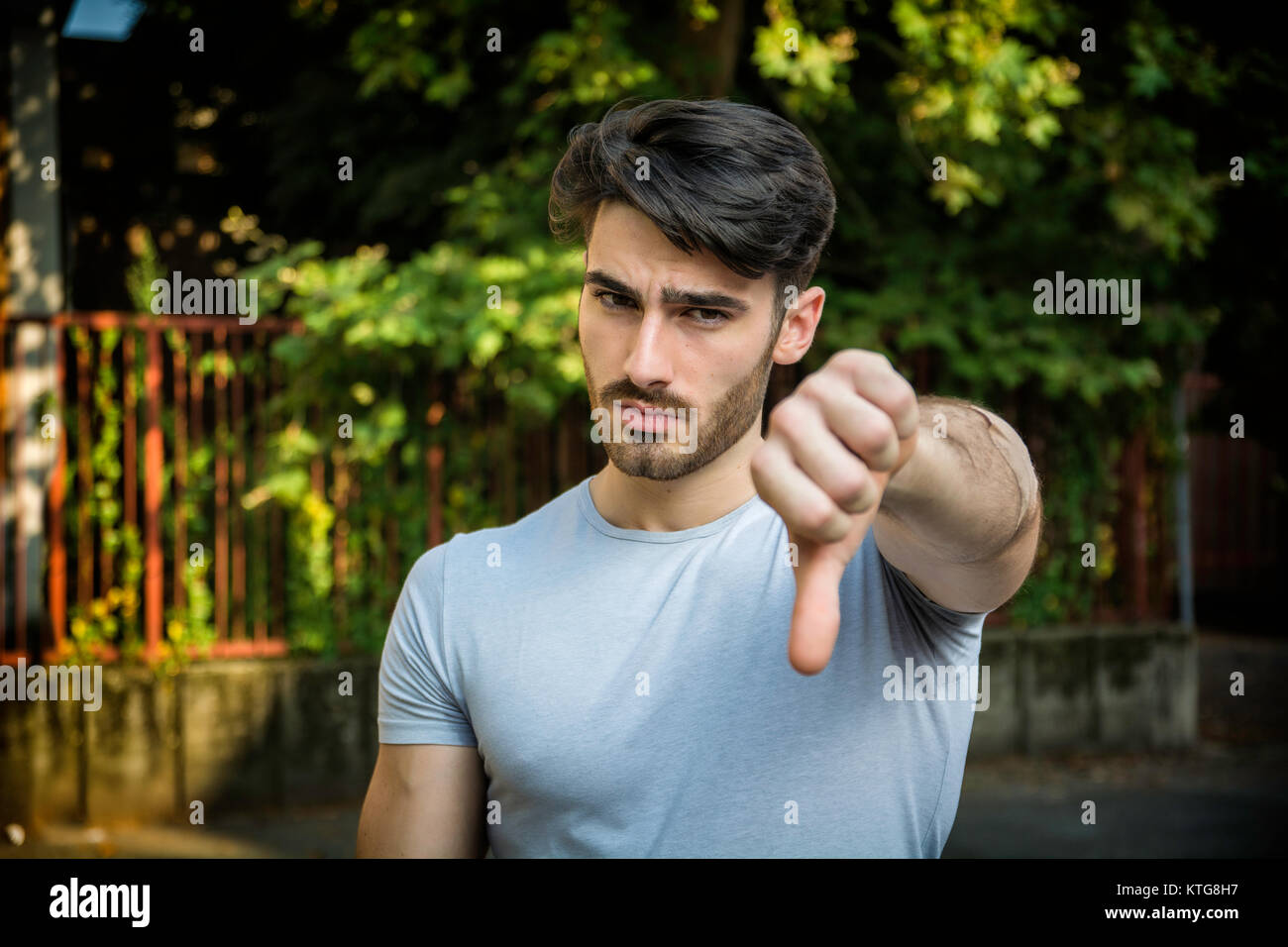 Handsome young man doing thumb down sign with hand, outside in city ...