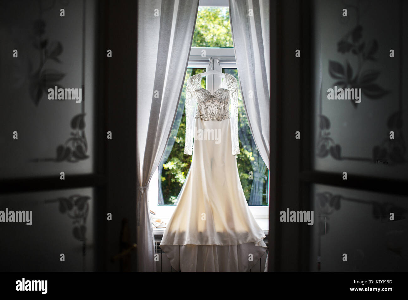 Wedding dress hanging on the window in the room Stock Photo - Alamy