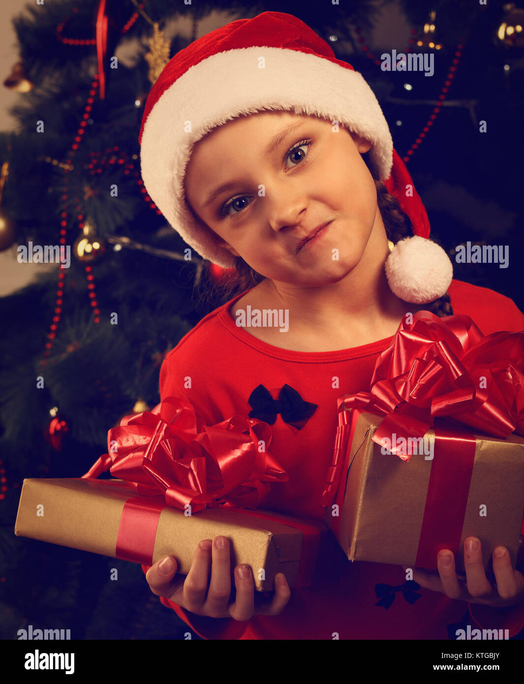Cute grimacing kid girl in Christmas santa claus hat holding the red ...