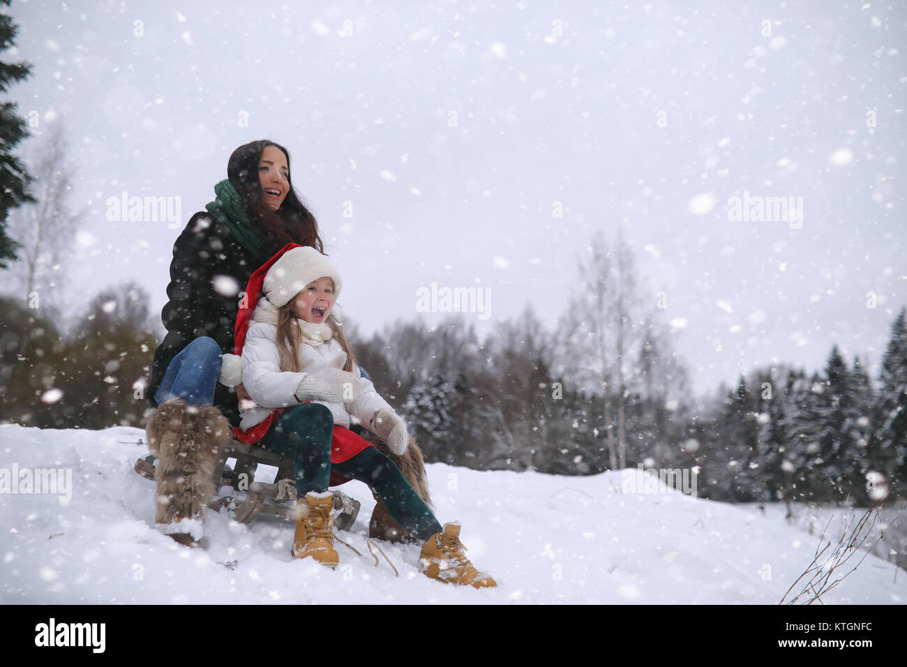 Winter fairy tale, a young mother and her daughter ride a sled in the ...