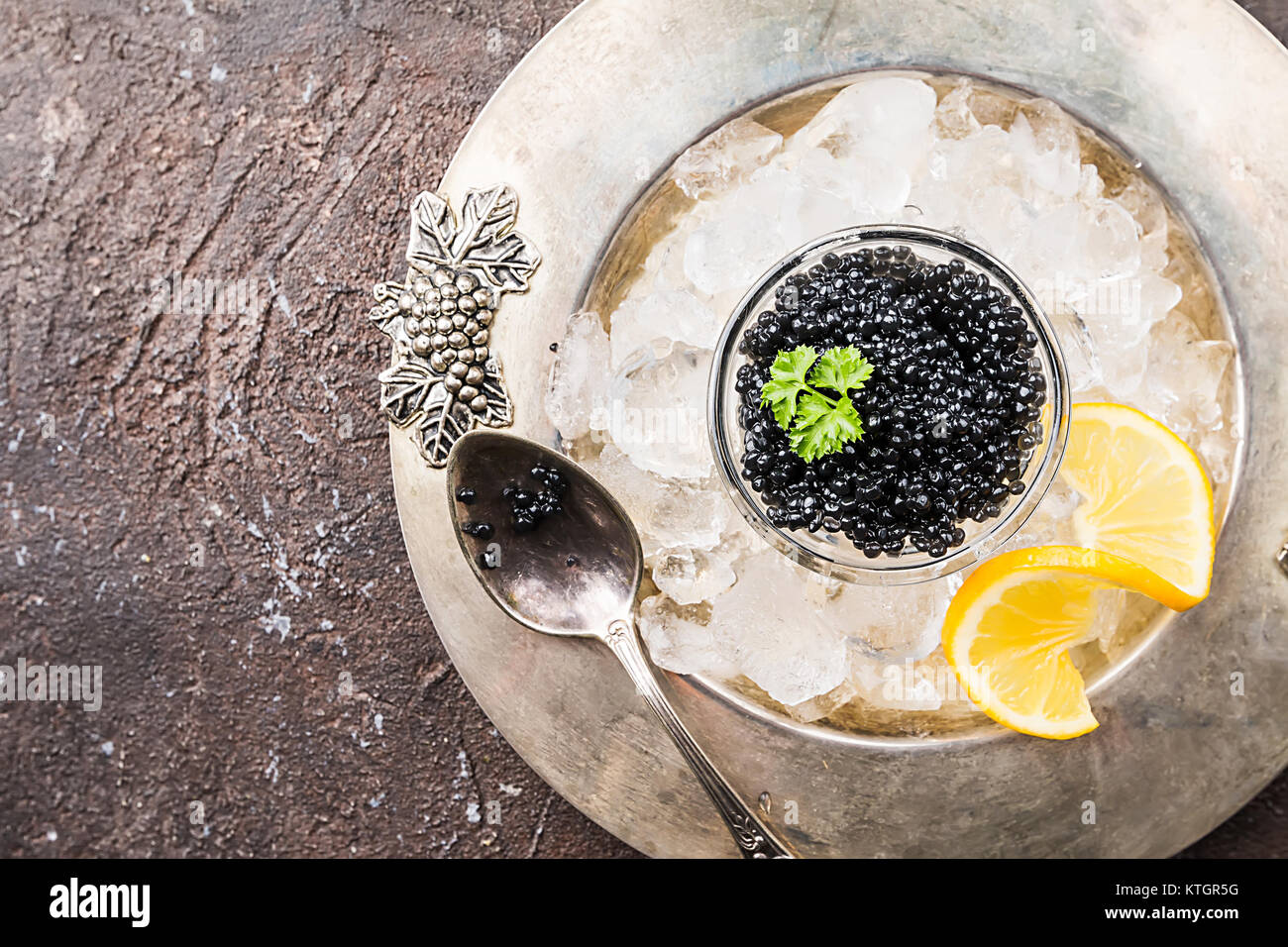 Black caviar in a glass bowl on ice with lemon close up over dark ...