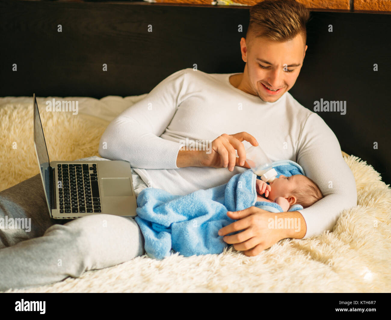 man feeding little baby while lying on bed and working on laptop Stock ...
