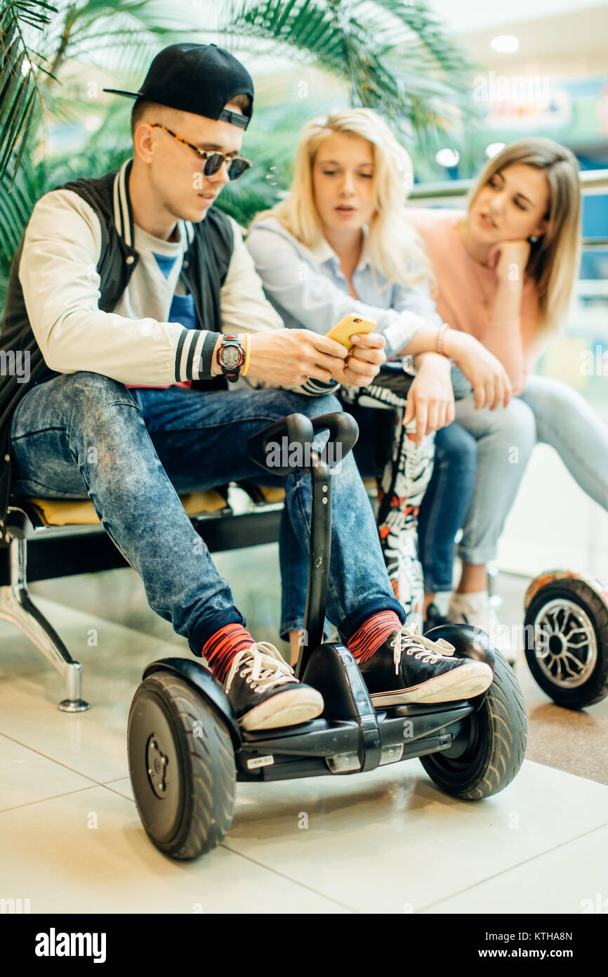 group of people on electric scooter hoverboard sitting at bench and ...