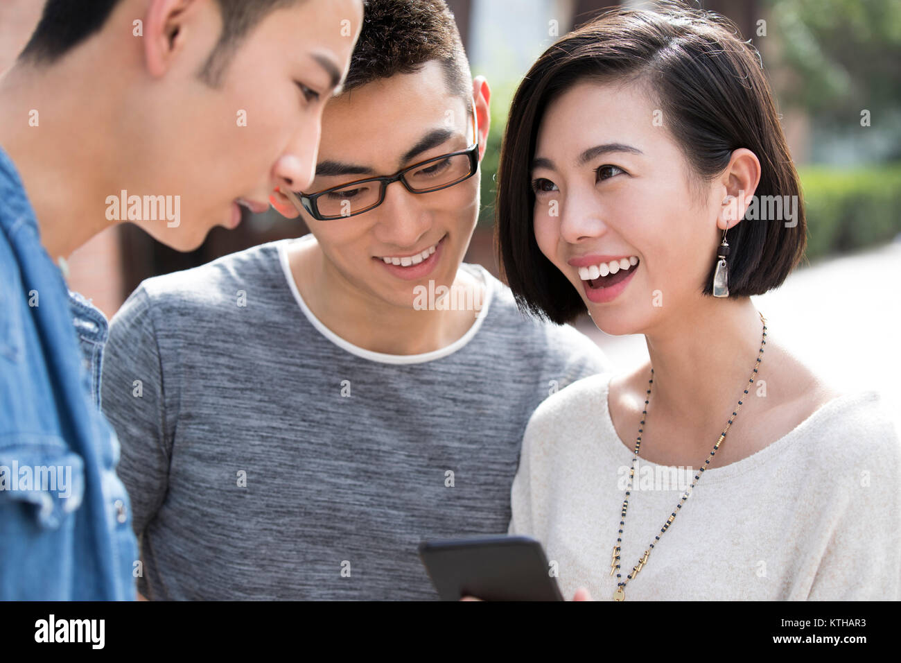 Cheerful young friends using smart phone Stock Photo - Alamy