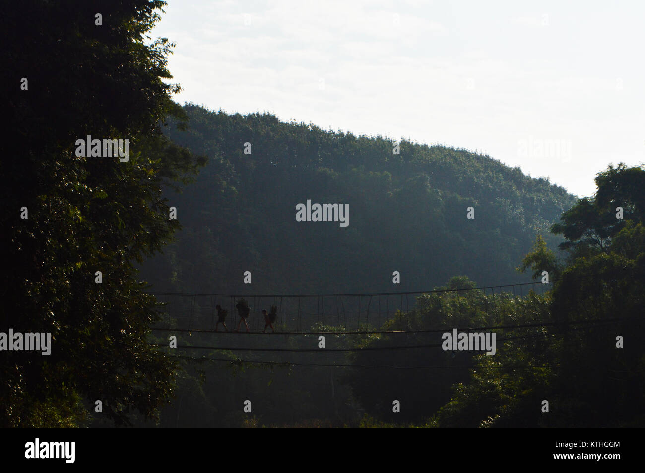 Three people crossing a river on a small rope bridge in Laos - Asia ...