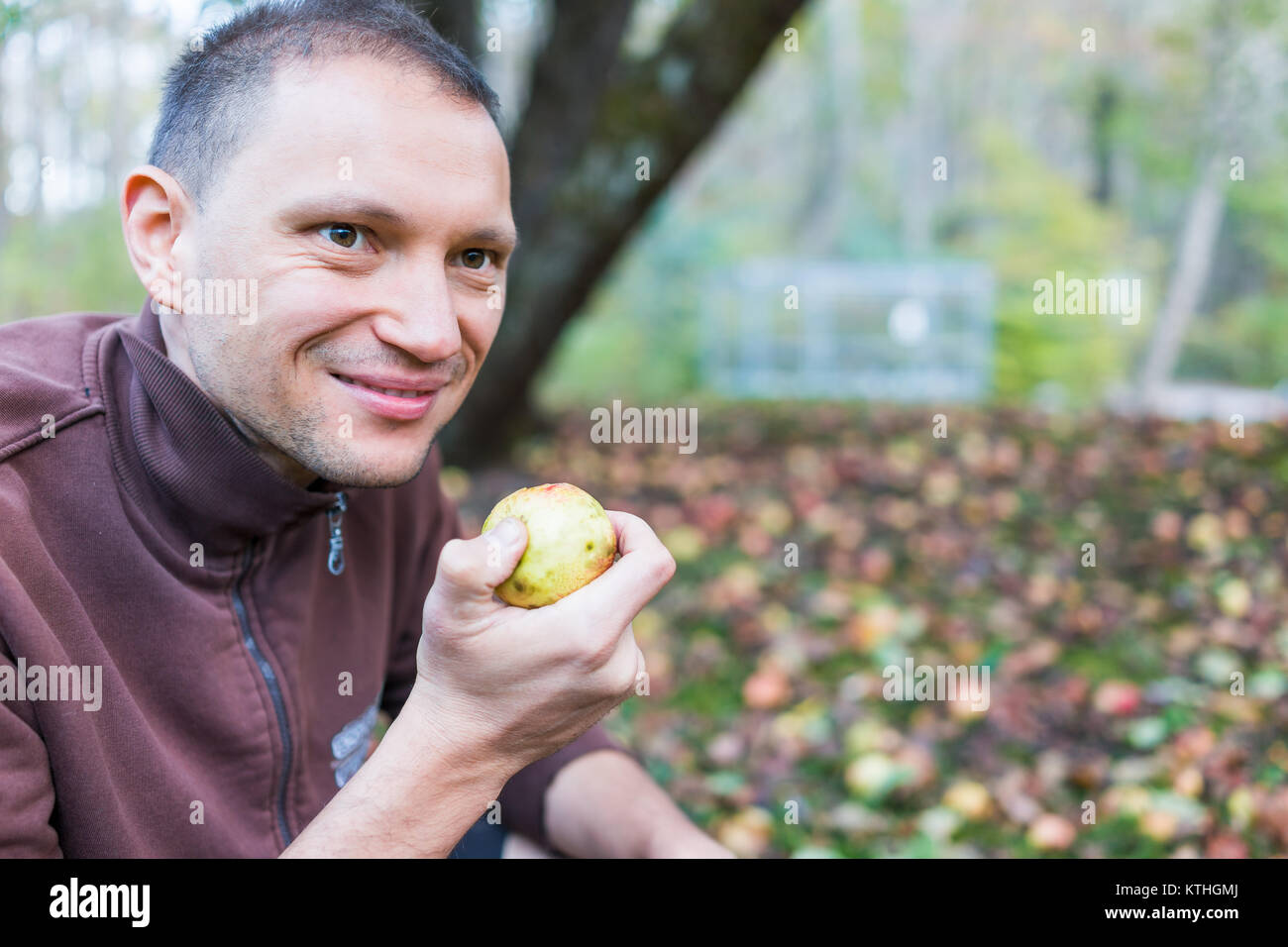 Smiling young man face eating one apple fallen wild fresh on grass ...
