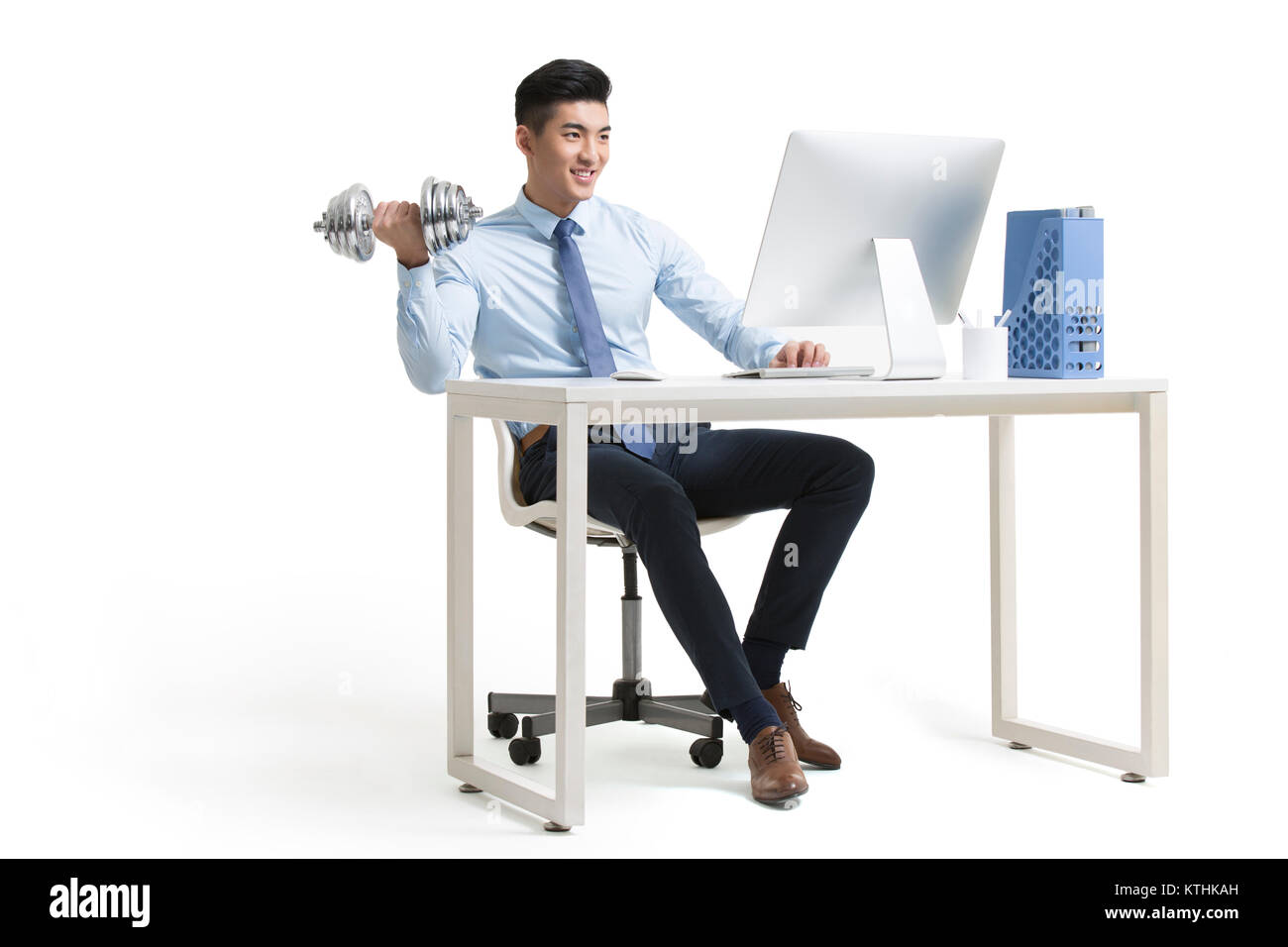 Young businessman lifting weights while using computer at work Stock ...