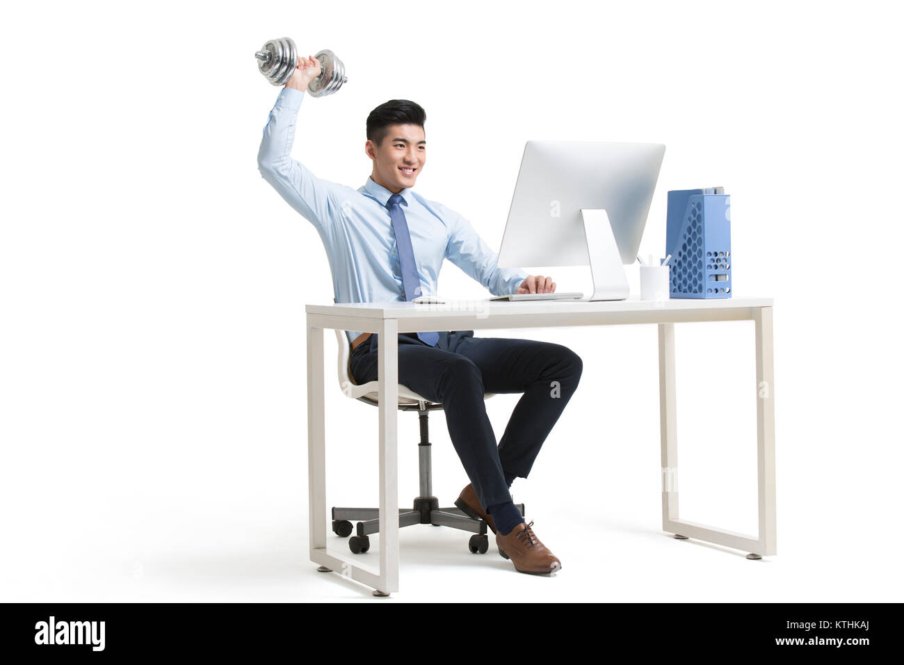 Young businessman lifting weights while using computer at work Stock ...