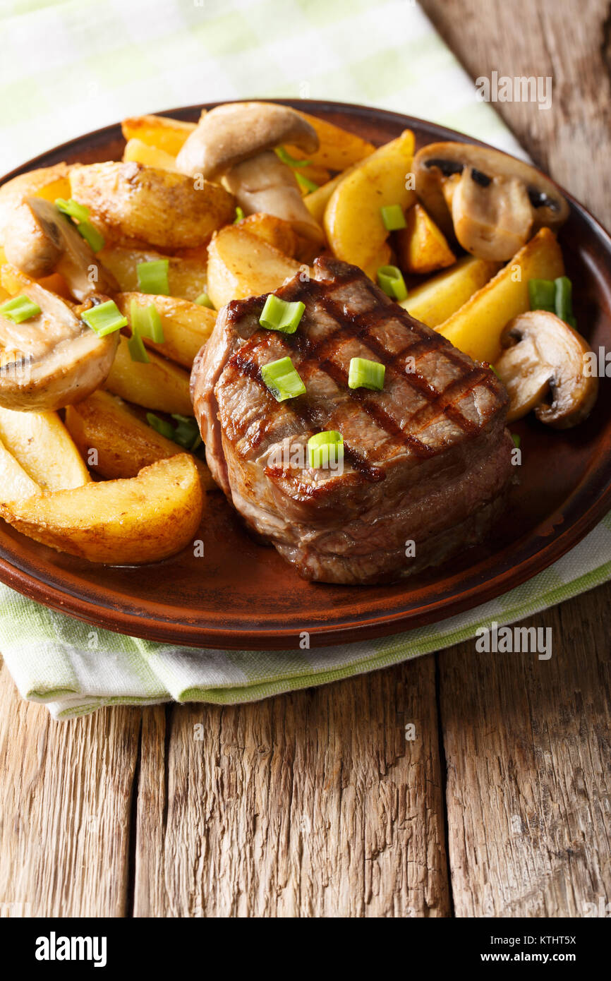 Grill fillet mignon with a garnish of potato wedges and mushrooms close ...
