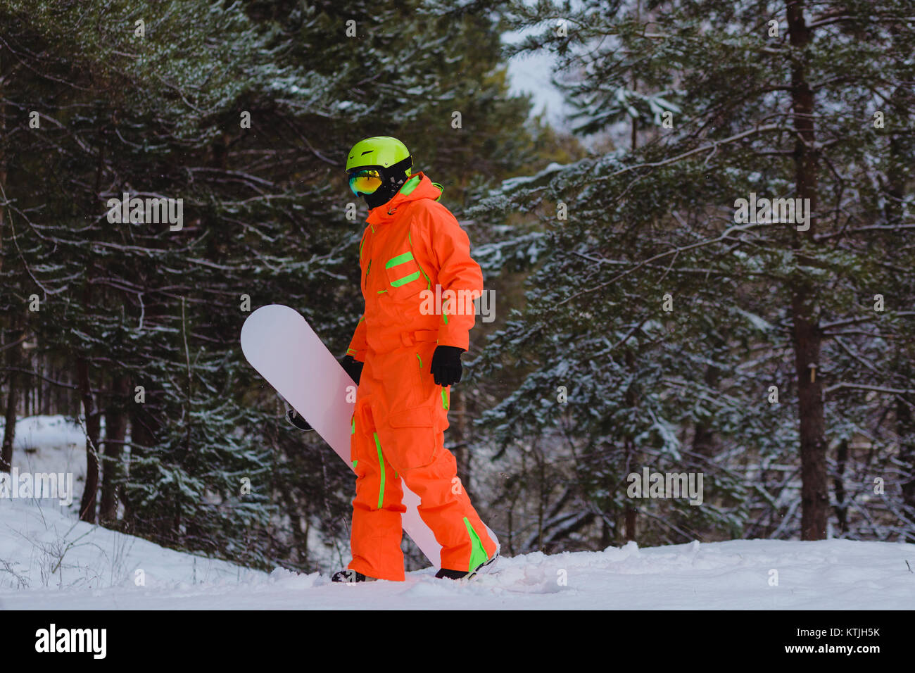 Snowboarder dressed in orange suit walking through the forest Stock ...