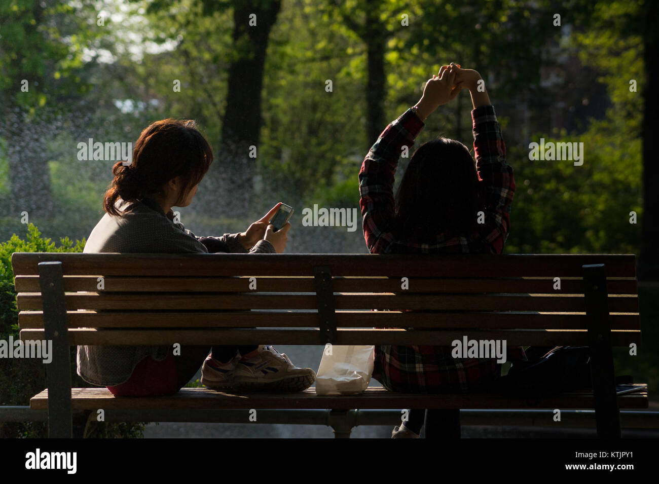 This image depicts a group of people sitting on a bench outdoors, using ...